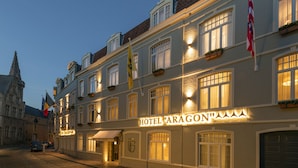 A historic building with a sign reading "HOTEL ARAGON." It features multiple windows and balconies with plants.