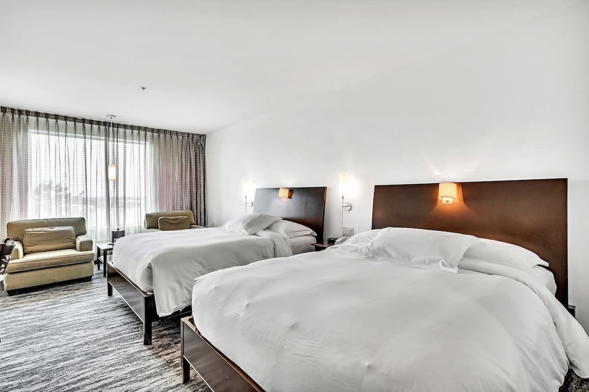 Quarto de hotel com duas camas, um sofá e uma janela grande com cortinas.