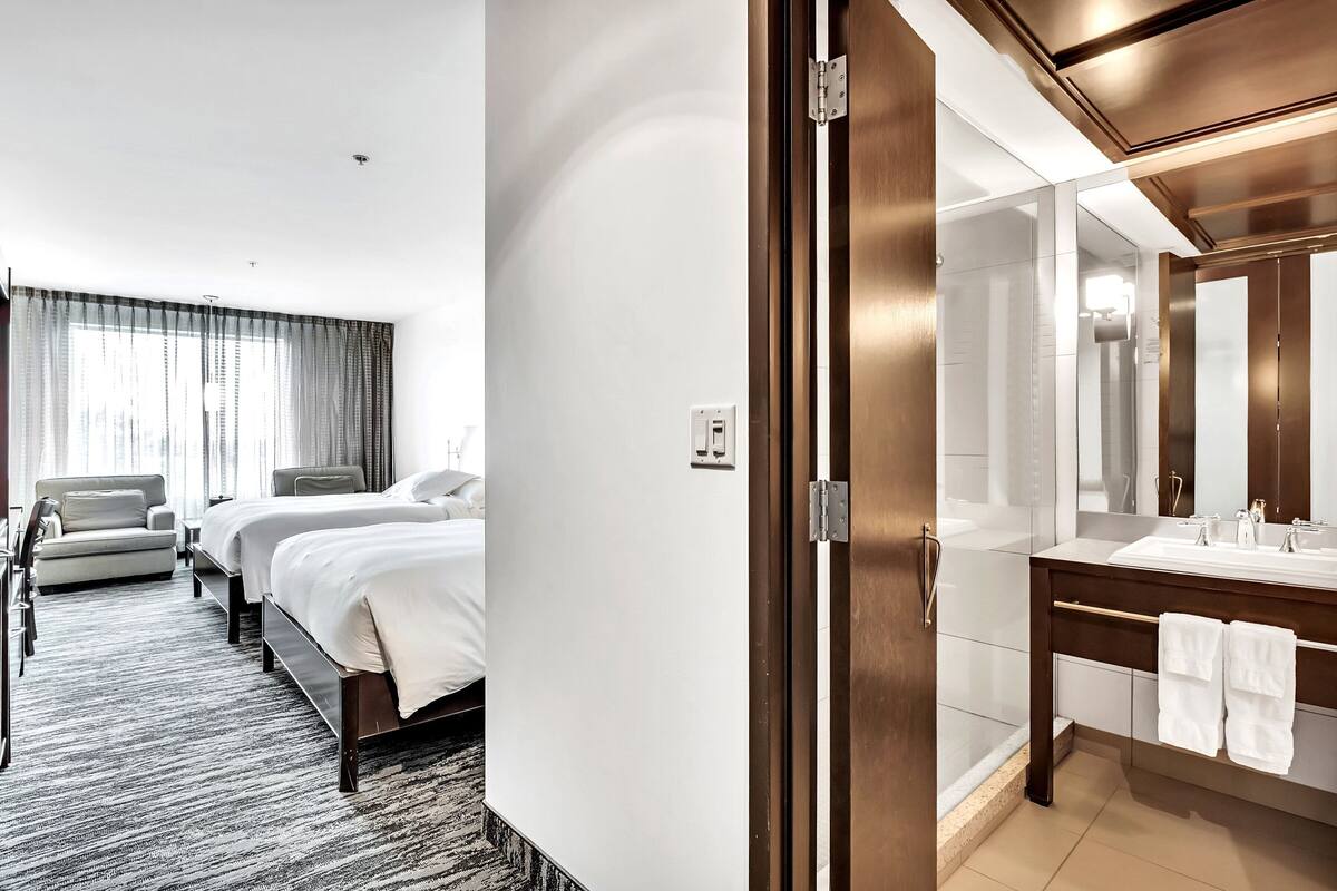 Quarto de hotel com cama, sofá, banheiro com espelho e chuveiro.