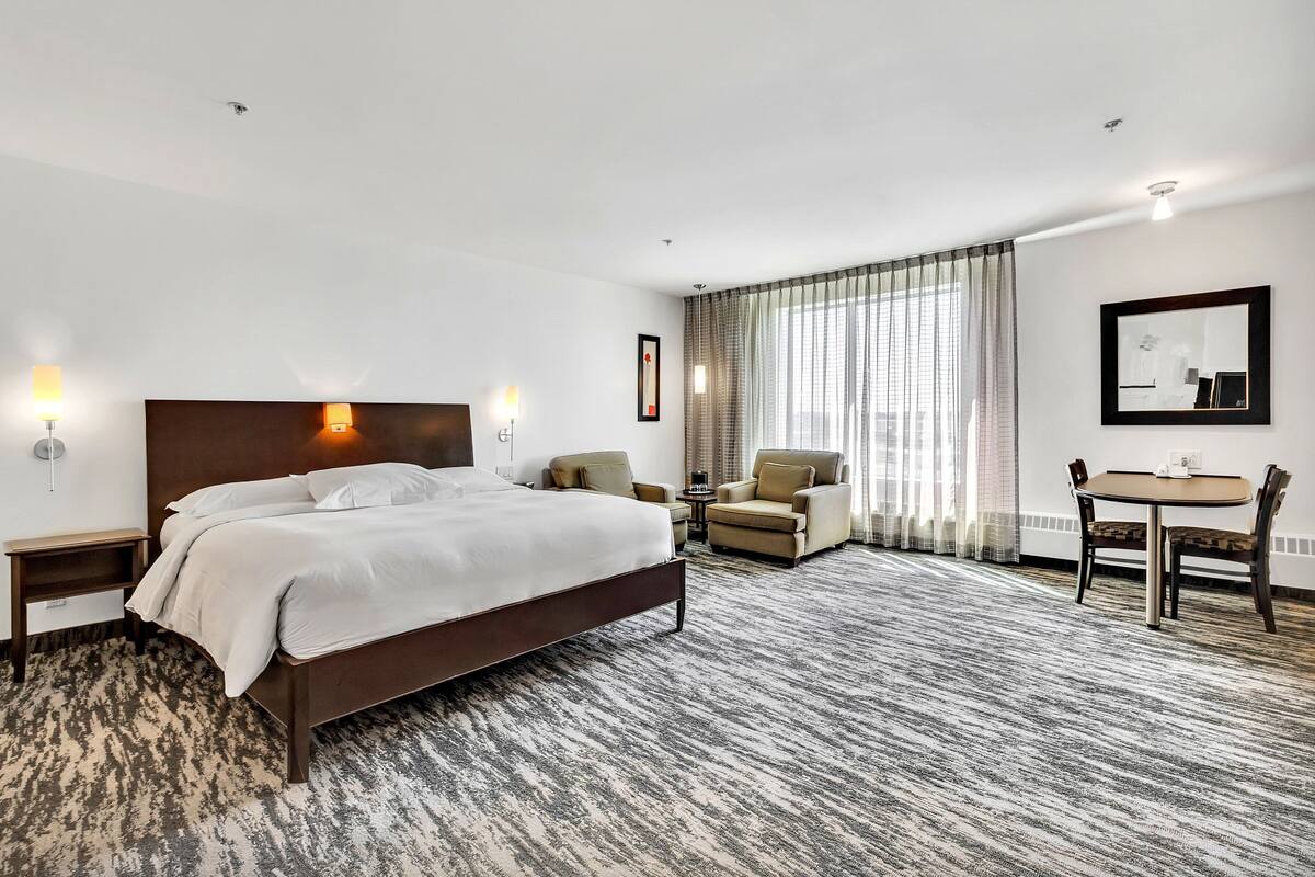 Quarto de hotel com uma cama grande, uma escrivaninha, dois poltronas e uma mesa de jantar.