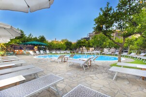 Uma área à beira da piscina com espreguiçadeiras, guarda-sóis e uma piscina.
