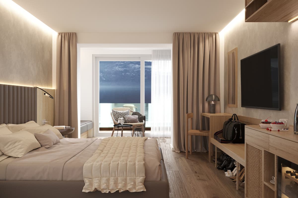 Quarto de hotel moderno com uma cama grande, uma escrivaninha com televisão, uma cadeira e vista para o mar.