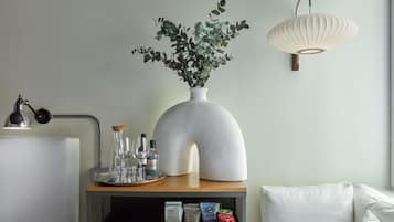 Uma sala de estar moderna com um sofá branco, uma mesa lateral de madeira com um vaso de plantas verdes, uma luminária e um acessório de iluminação fixado na parede.