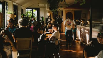 Um espaço amplo e movimentado para refeições no interior, com piso de madeira, plantas em vasos e um balcão de bar.
