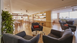 Um hall amplo com mobiliário moderno, um espaço de bar e janelas grandes.