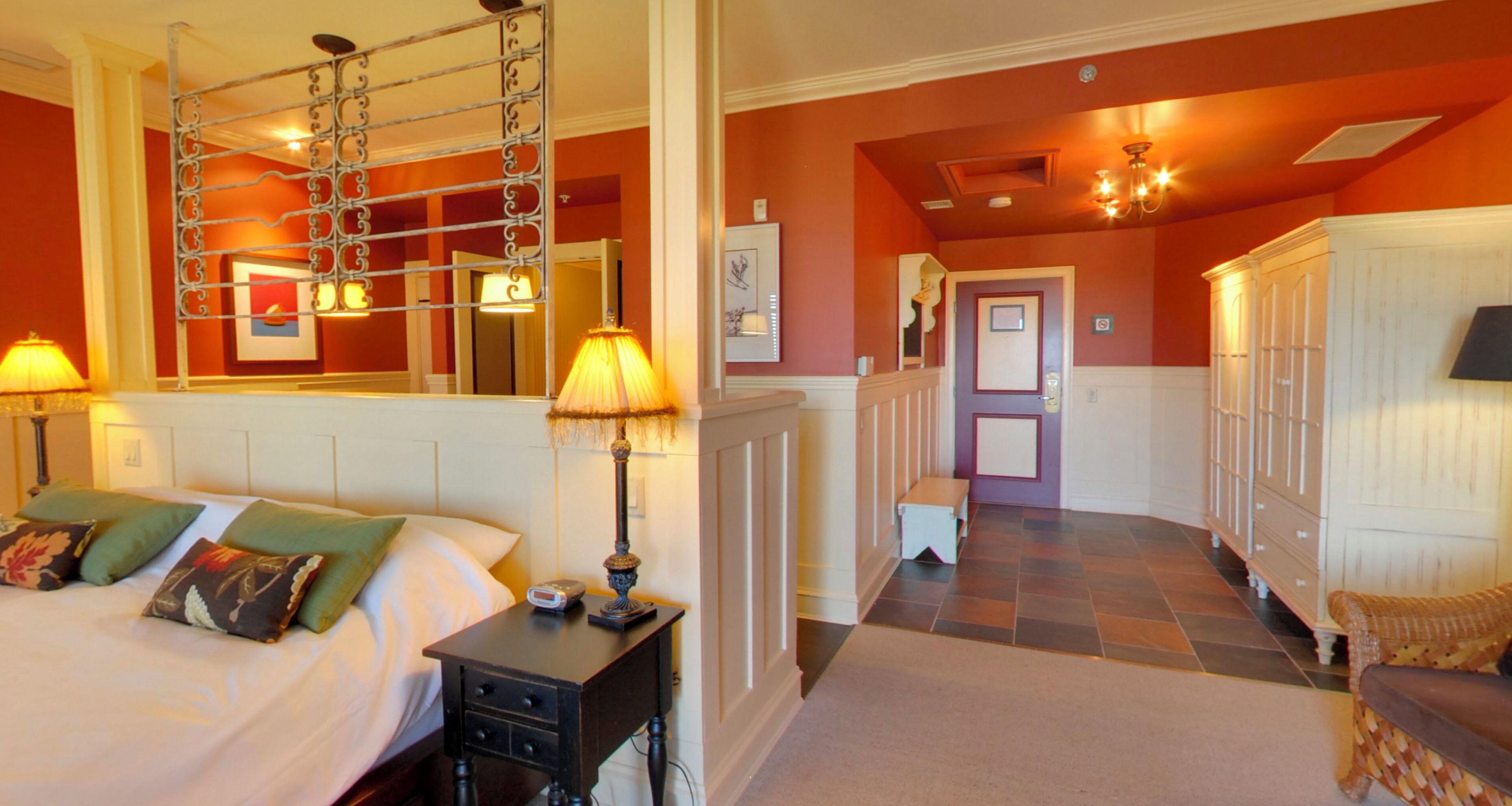 Quarto de hotel com cama, mesa de cabeceira, abajur e guarda-roupa.