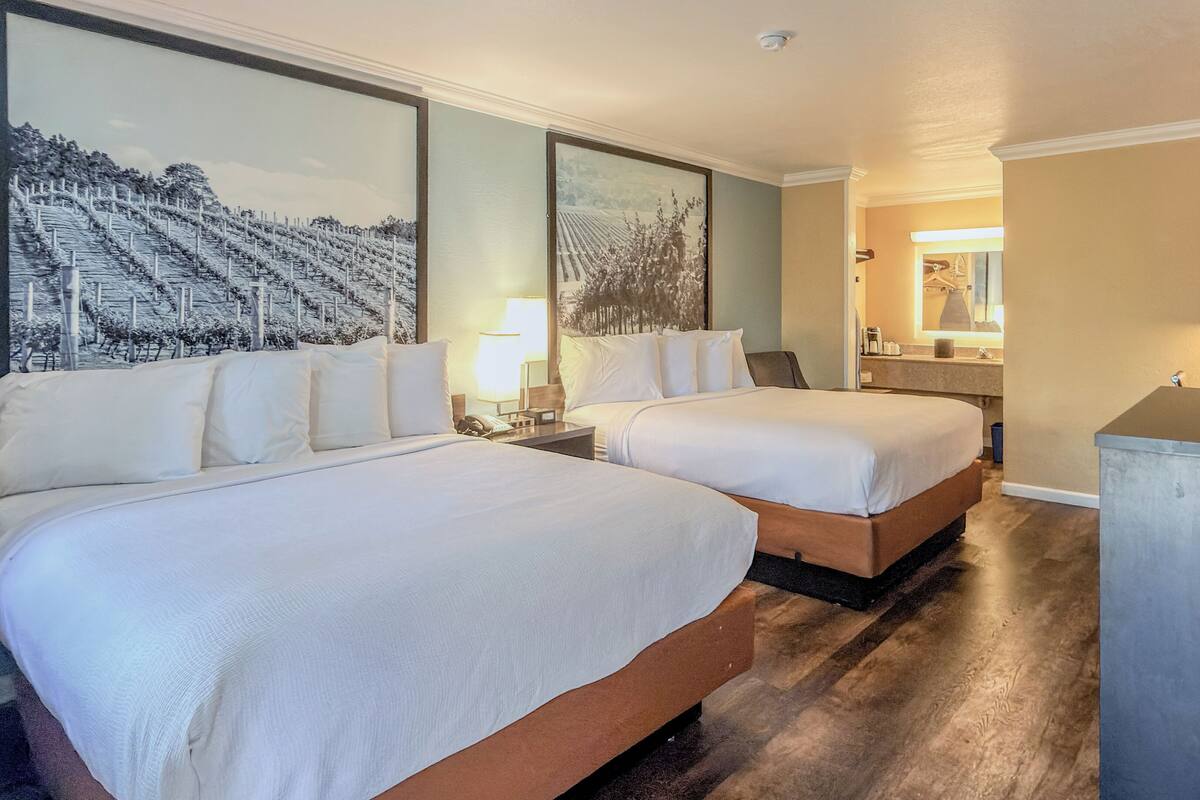 Quarto de hotel com duas camas, um espelho grande, piso de madeira e vista para um vinhedo.