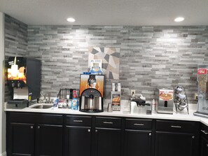 Uma cozinha moderna com painel de pedra, máquina de café, dispensador de suco de frutas e chaleira.