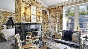 Quarto com lareira, sofá, poltrona e mesa com livros.