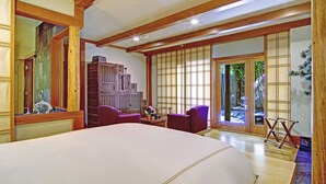 Um quarto espaçoso com uma cama grande, vigas de madeira, uma porta tradicional japonesa deslizante e uma pequena mesa com cadeiras.