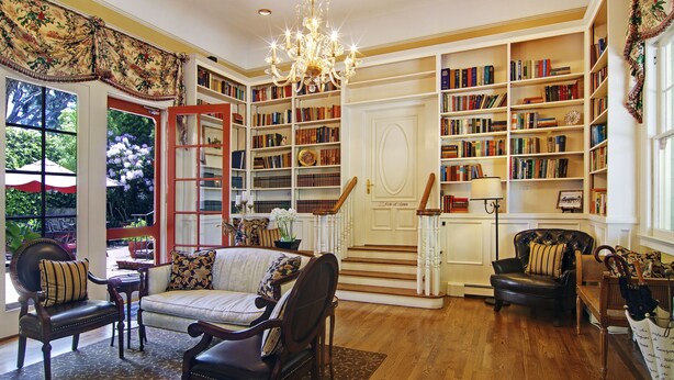 Uma biblioteca com estantes, um candelabro e uma lareira.
