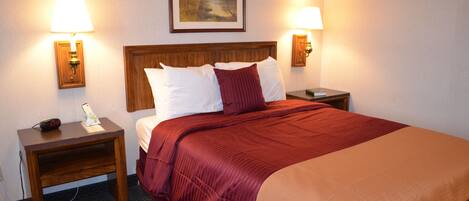Quarto de hotel com uma cama grande, duas mesas de cabeceira, um criado-mudo, um quadro na parede e duas luminárias de parede.