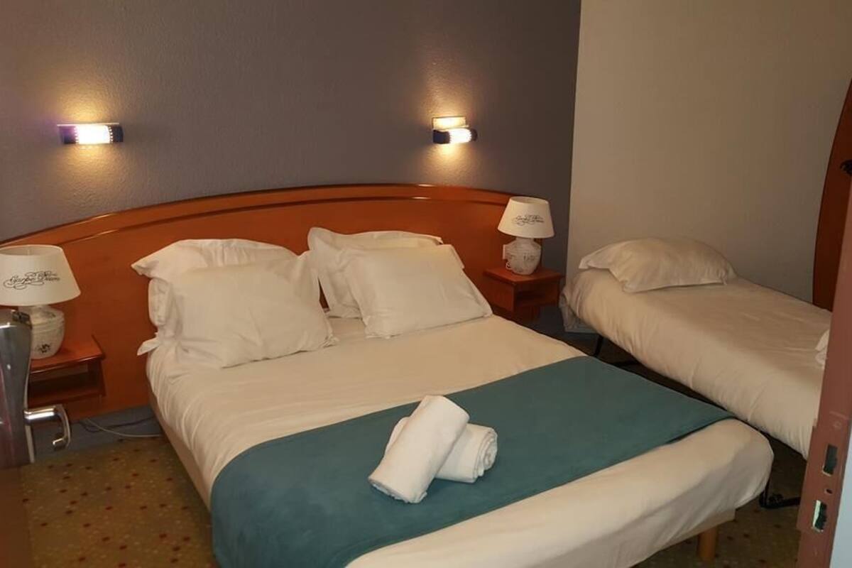 Quarto de hotel com duas camas, cabeceira de madeira, abajures e cobreleite azul-esverdeado.