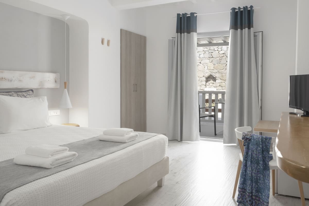Quarto de hotel moderno com cama, escrivaninha e varanda com cortinas.