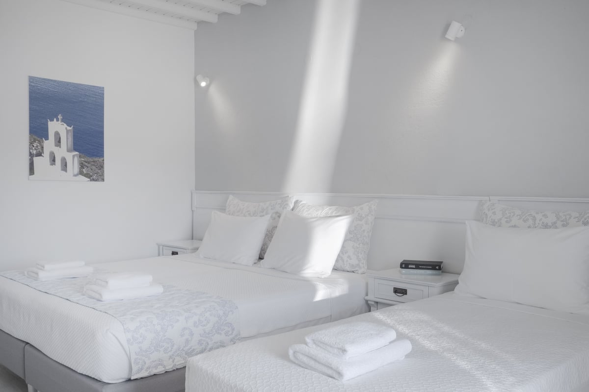 Quarto de hotel com duas camas, roupa de cama branca, mesa de cabeceira com telefone e pintura de um edifício costeiro.