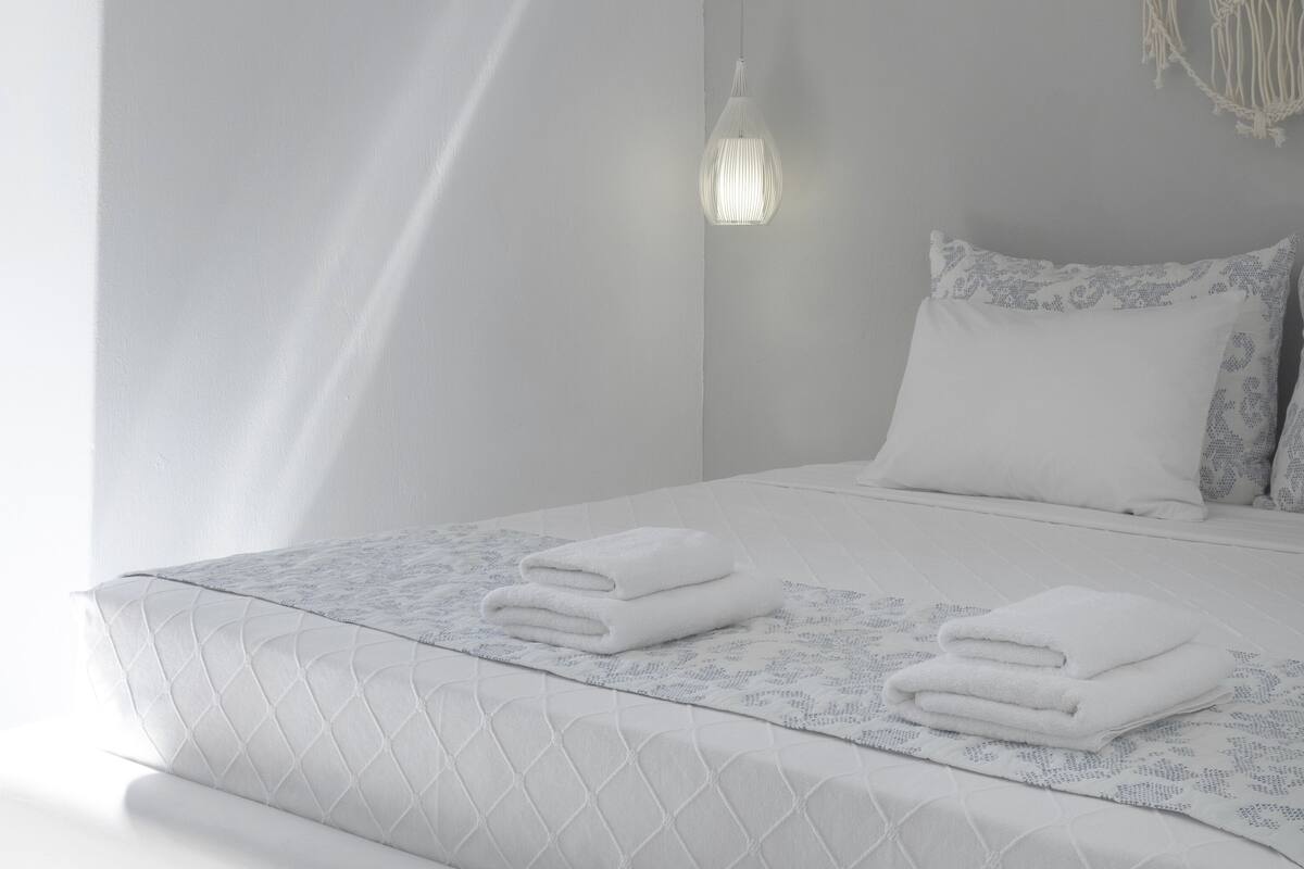 Quarto minimalista com uma cama, um painel de macramé e uma luminária pendente.