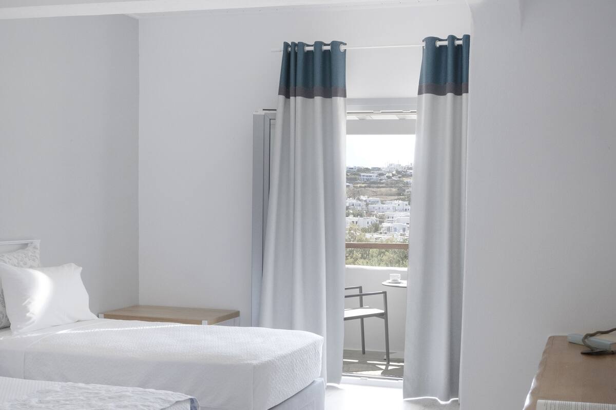 Quarto com duas camas, uma escrivaninha e vista para a cidade.