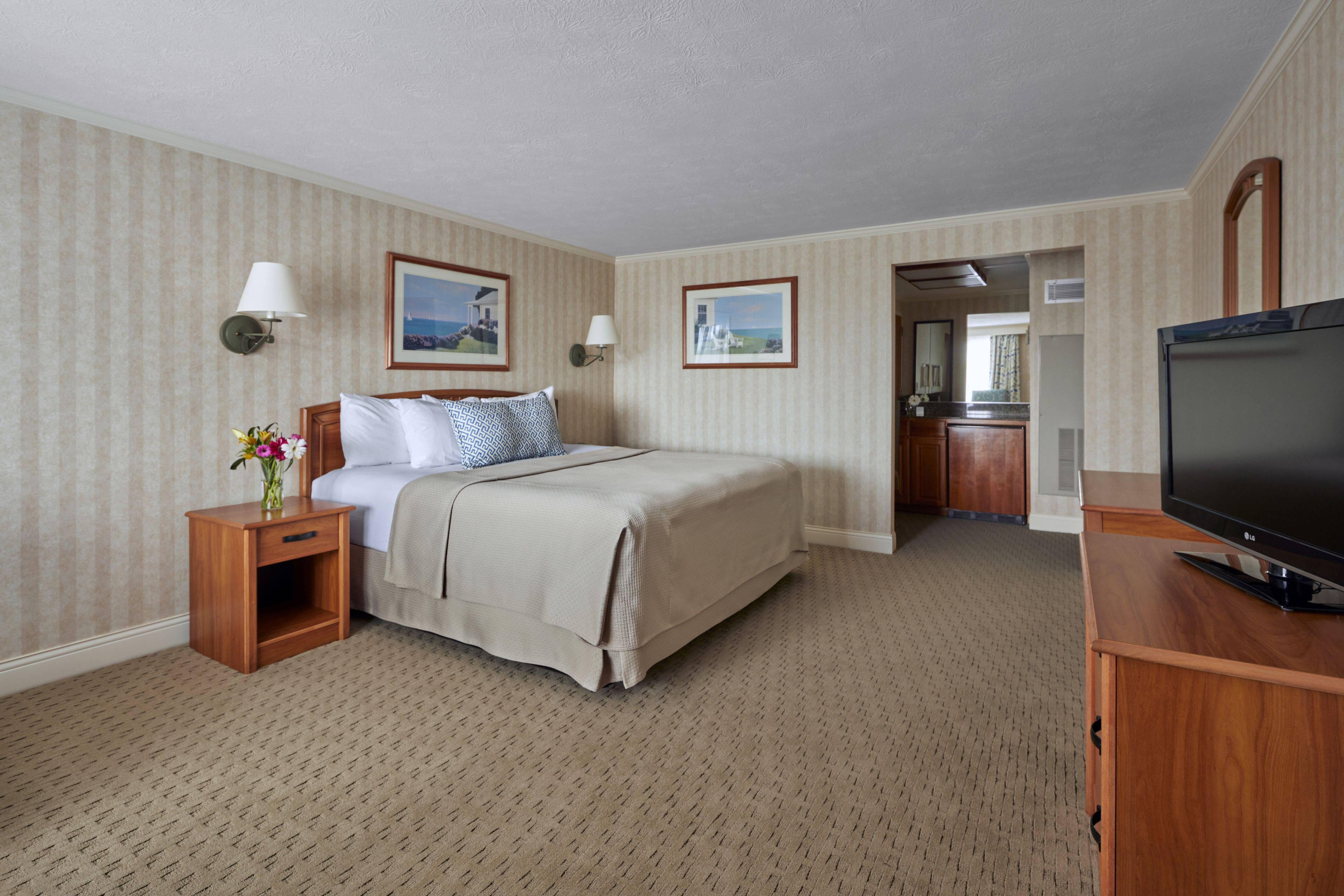 Quarto de hotel com cama, mesas de cabeceira, televisão e cozinha compacta.