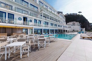 Convés de navio de cruzeiro com área de estar externa, piscina e vista da paisagem ao redor.