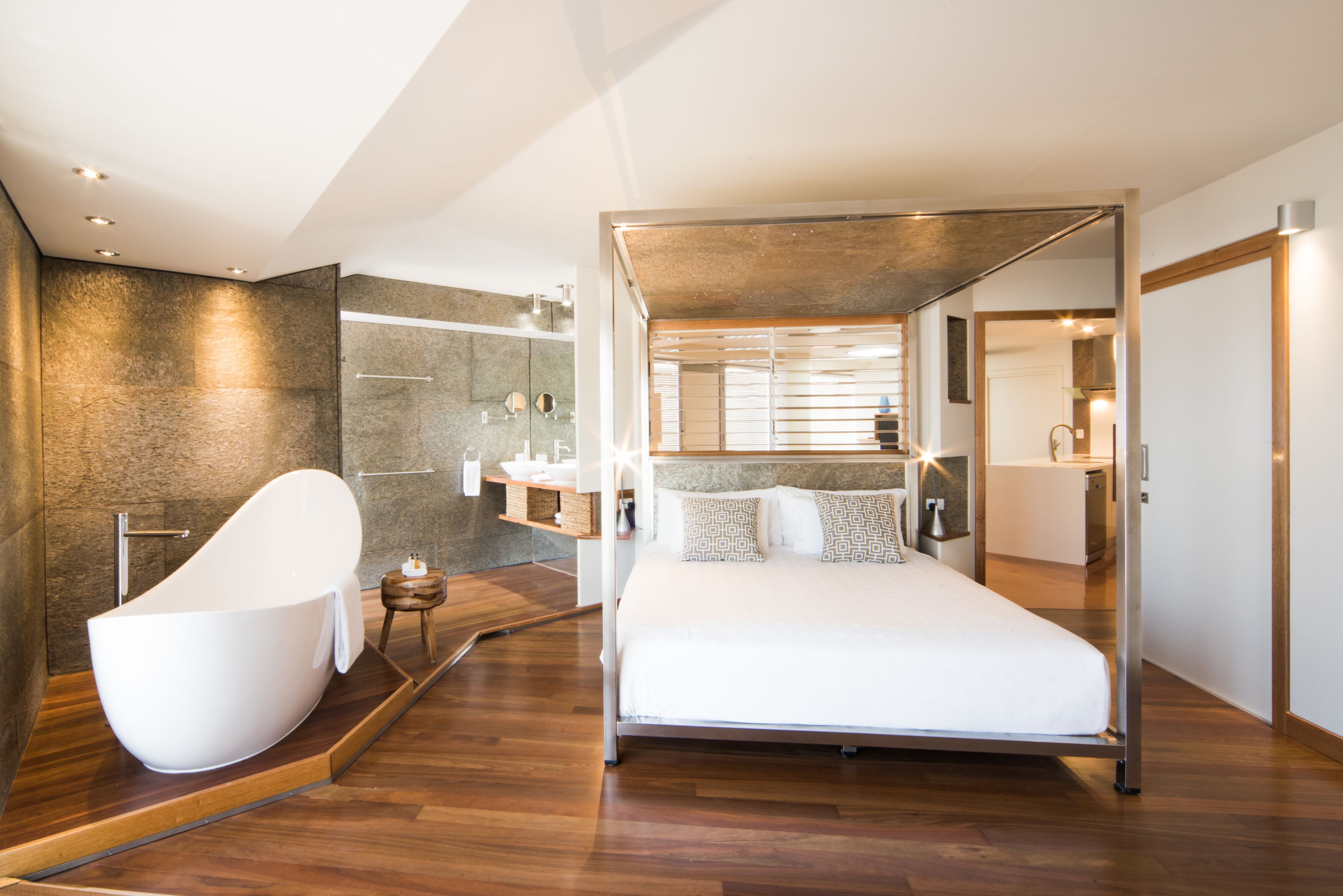 Um quarto moderno com uma cama grande, uma banheira independente e um chuveiro amplo.