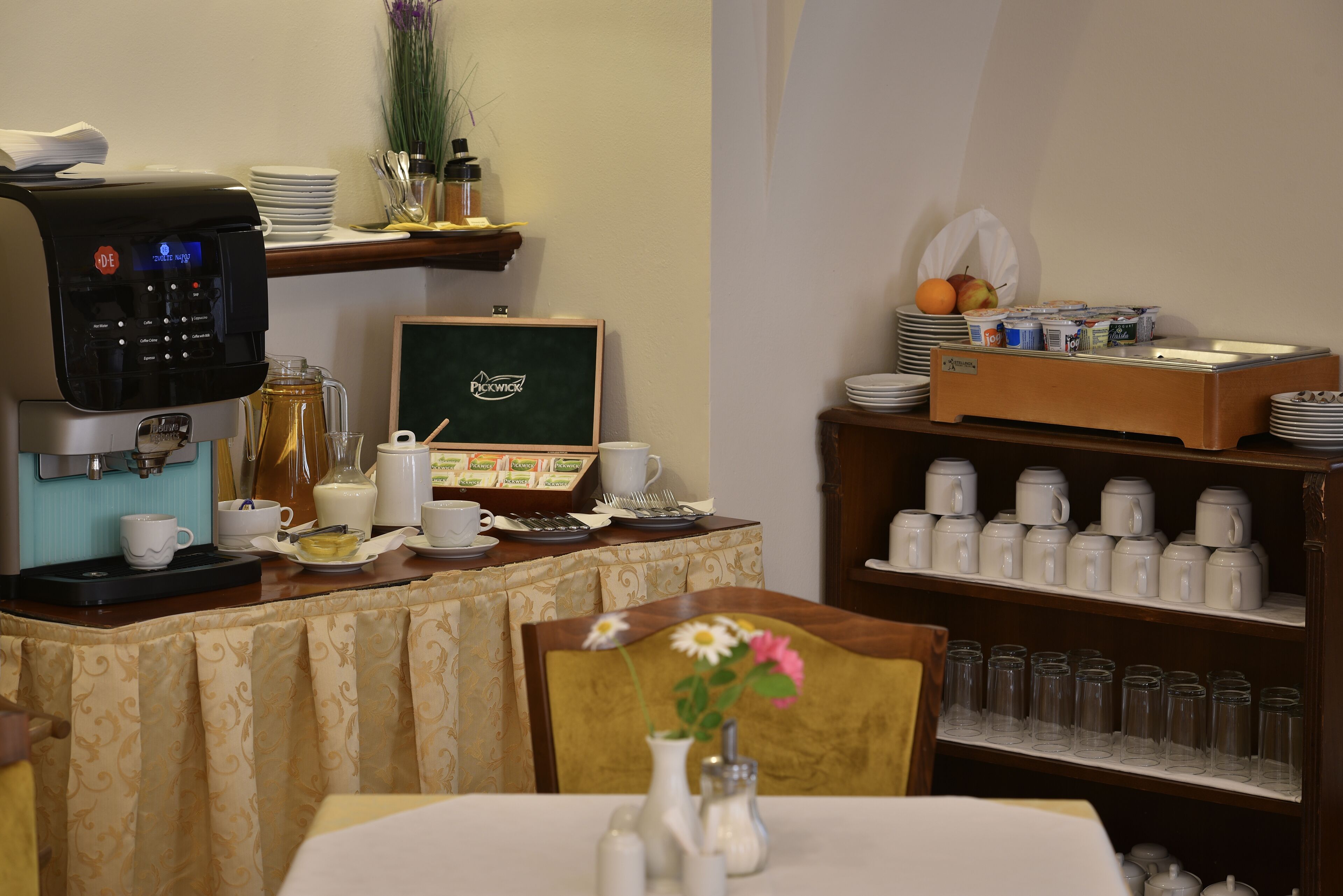 Disposição para o café da manhã com uma cafeteira, chaleira e diversos copos e canecas em prateleiras.