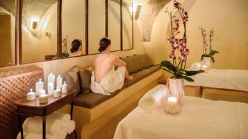 Uma sala de spa com mesa de massagem, área de estar com sofá e mesa com velas e toalhas.