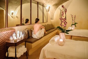 Uma sala de spa com mesa de massagem, área de estar com sofá e mesa com velas e toalhas.