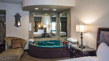 Quarto de hotel com cama grande, área de estar curvilínea, hidromassagem, toucador com espelho e luminária.