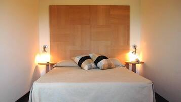 Cama bem arrumada com cabeceira de madeira, duas luminárias de apoio e um espalha-cama em tons neutros.