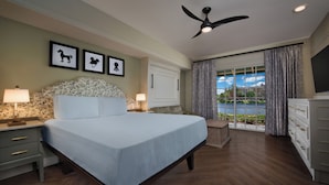 Quarto com cama, mesas de cabeceira, ventilador de teto, quadros nas paredes, janela com vista e cômoda.