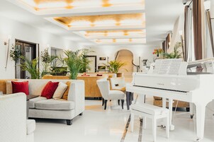 Um hall de hotel moderno com um piano de cauda, balcão de recepção e áreas de estar confortáveis.