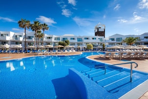 Piscina com espreguiçadeiras e guarda-sóis, cercada por edifícios modernos com varandas.