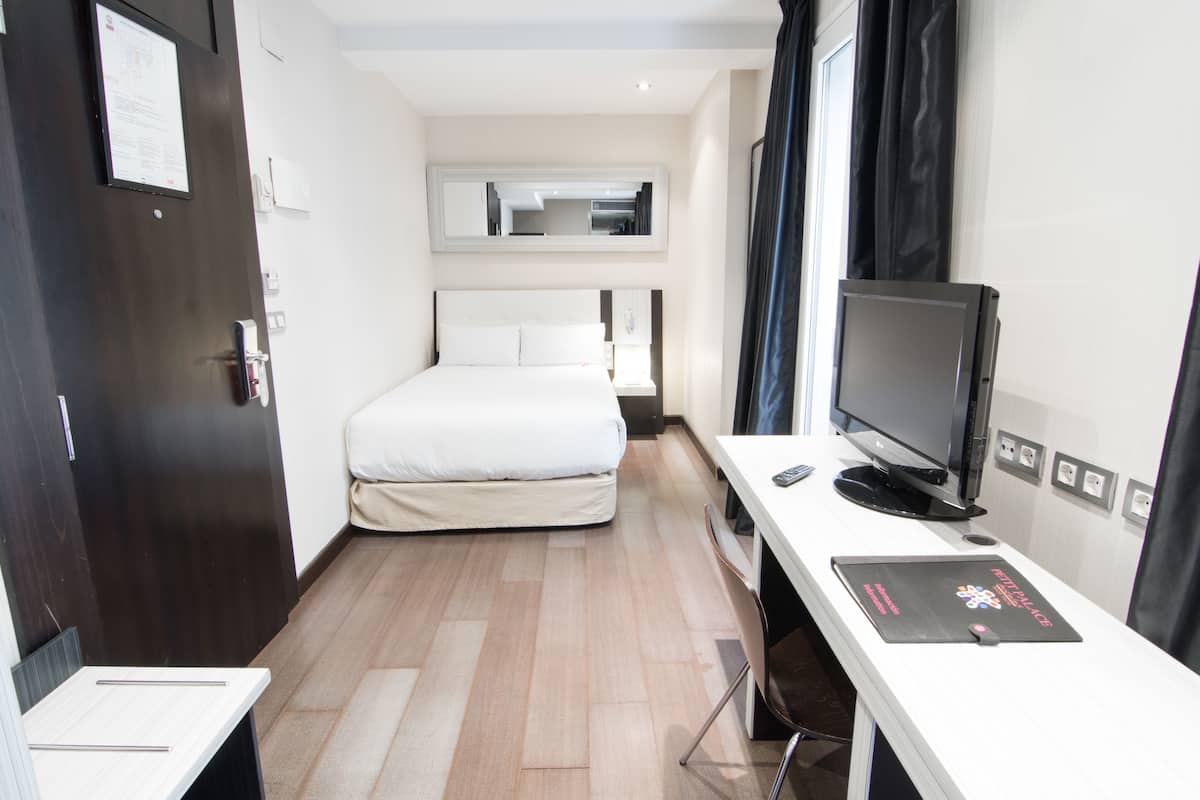 Quarto de hotel com cama, escrivaninha com computador, espelho e porta.