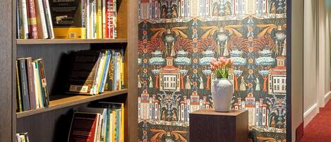 Uma biblioteca com estantes, um papel de parede estampado e um vaso com flores.