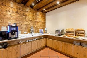 Um balcão de café da manhã com máquinas de café, espaço para chás e diversos pães e doces.