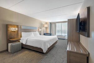 Quarto de hotel com uma cama grande, mesa de cabeceira, luminária, televisão e vista para o exterior pela janela.