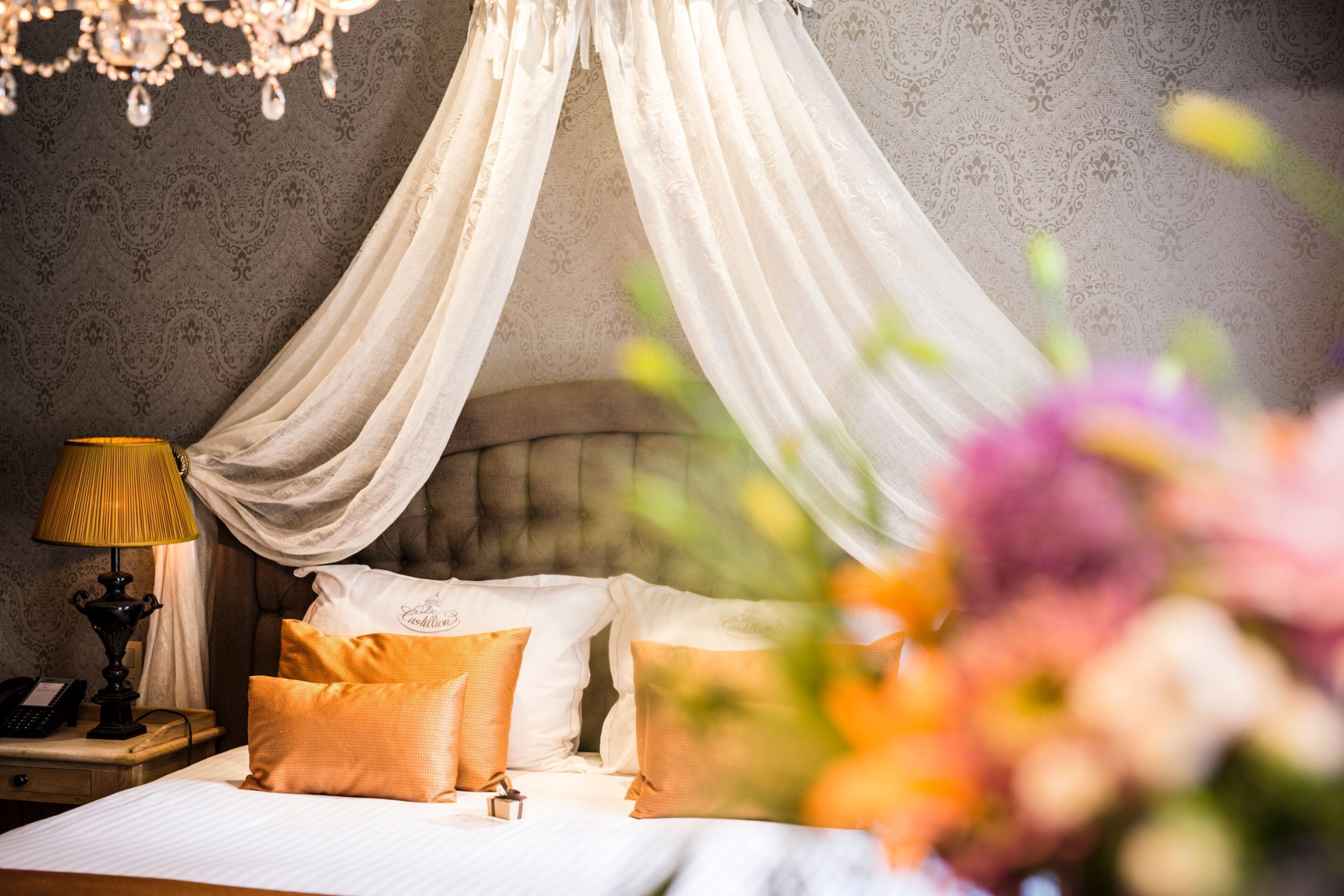 Quarto com cama de dossel, luminária de cabeceira e um arranjo floral.