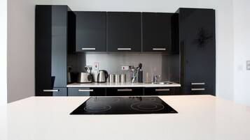 Uma cozinha moderna com armários pretos, bancada branca e fogão por indução preto.
