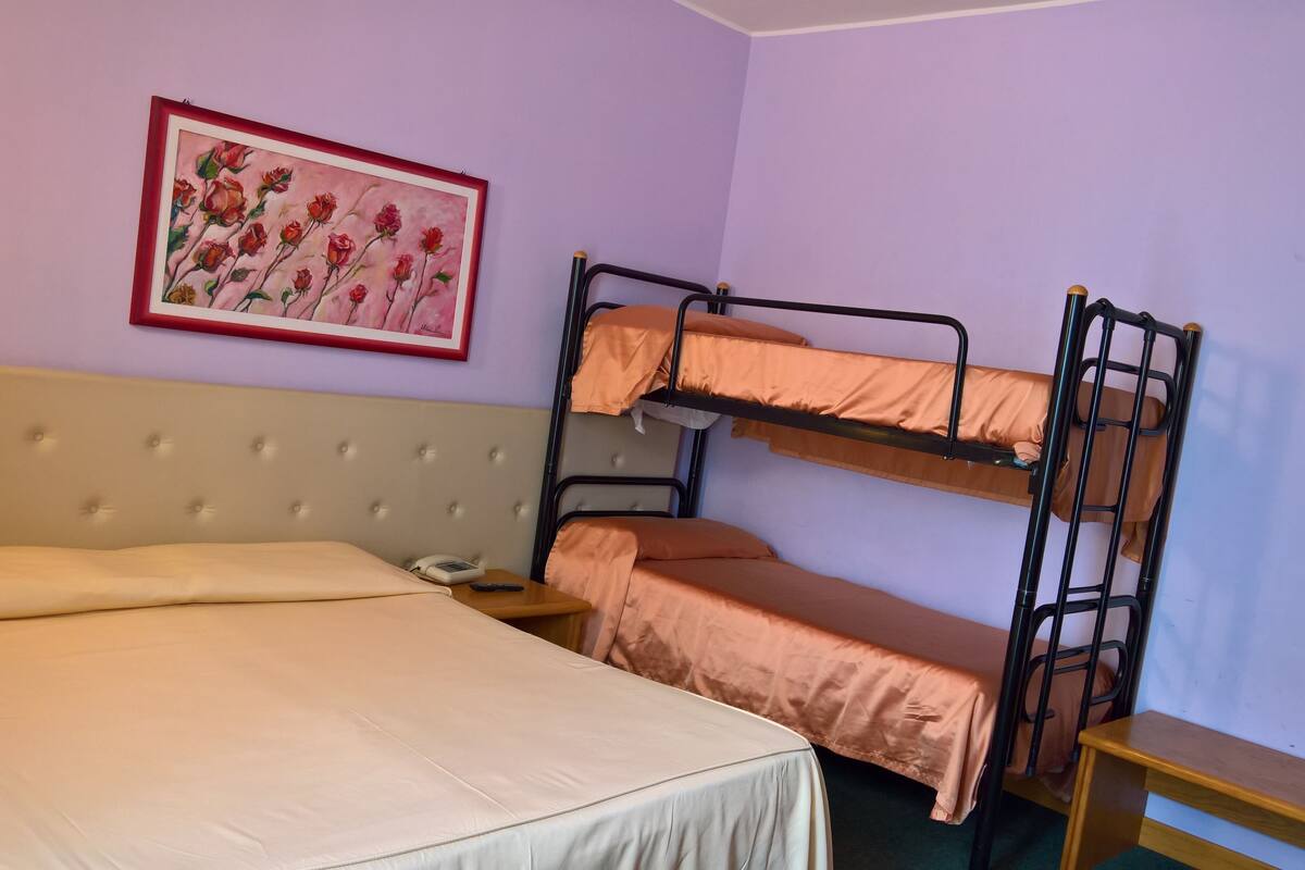 Quarto com uma cama de solteiro, uma cama beliche, uma mesa de cabeceira com telefone e um quadro floral na parede.