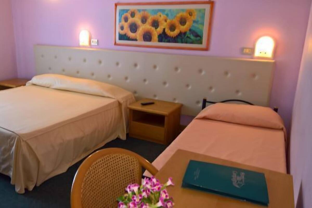 Quarto de hotel com duas camas, cabeceiras, mesas de cabeceira, uma cadeira e um quadro de girassóis.
