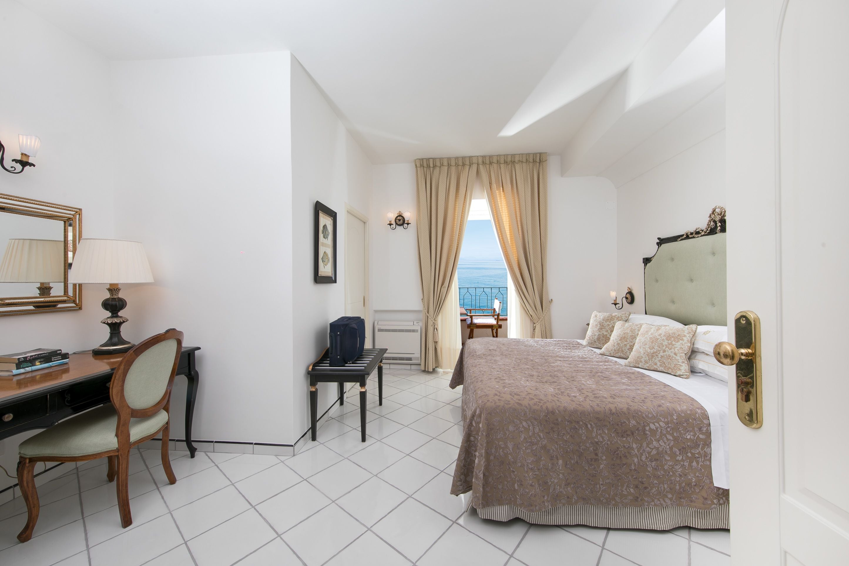 Quarto de hotel com cama, escrivaninha, cadeira e vista para o mar.
