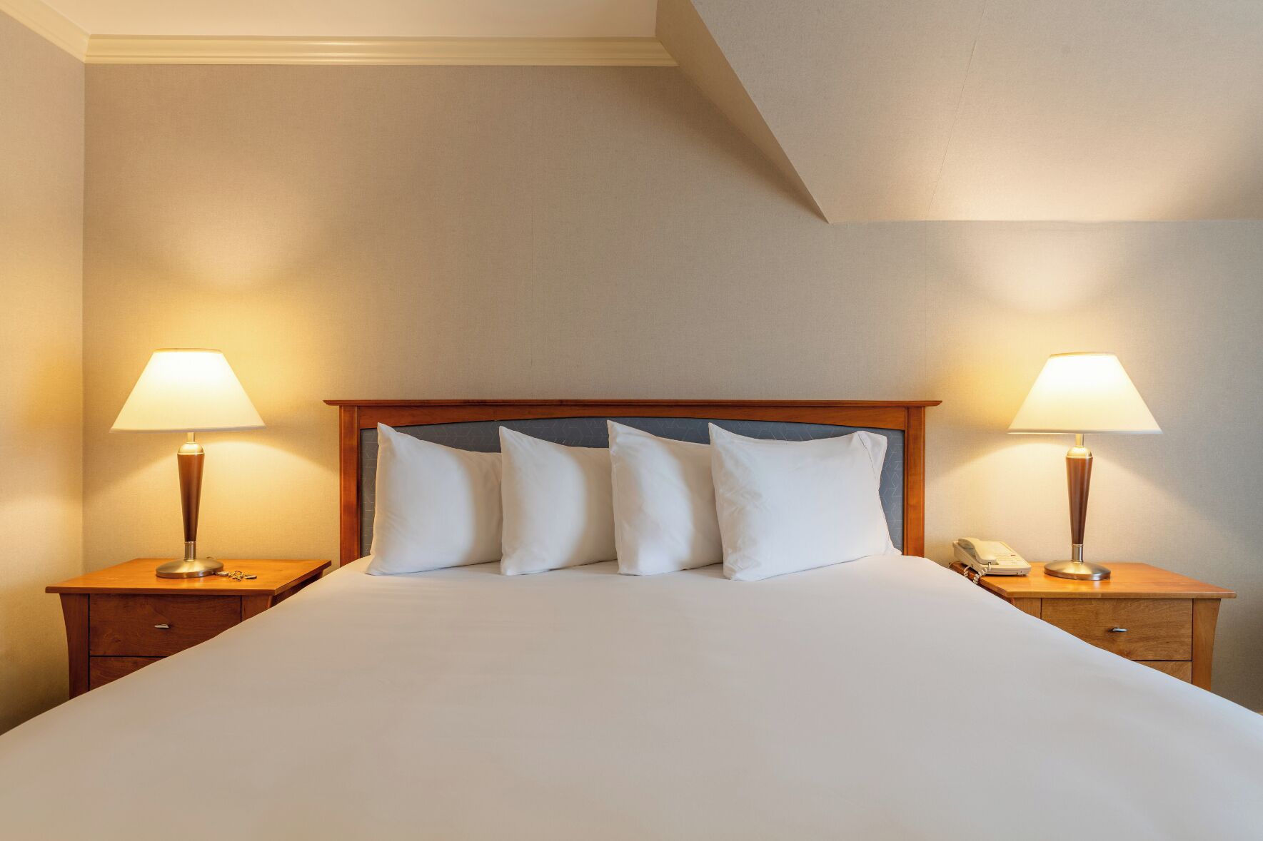 Uma cama bem arrumada com cabeceira de madeira, duas mesas de cabeceira com abajures e um telefone em uma delas.