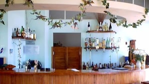 Uma área de bar com taburetes de madeira, prateleiras com garrafas e plantas penduradas.