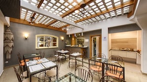 Uma sala de jantar com mesas e cadeiras, uma cozinha ao fundo e um teto com claraboias.