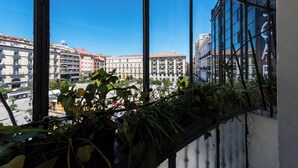 Vista da janela com varanda, sobre um quarteirão de prédios sob um céu azul e límpido.