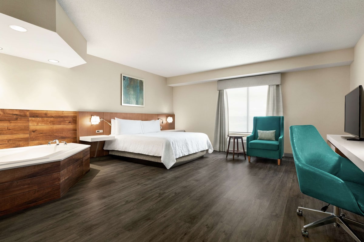 Quarto de hotel com cama grande, banheiro separado com banheira, escrivaninha com cadeira e televisão.
