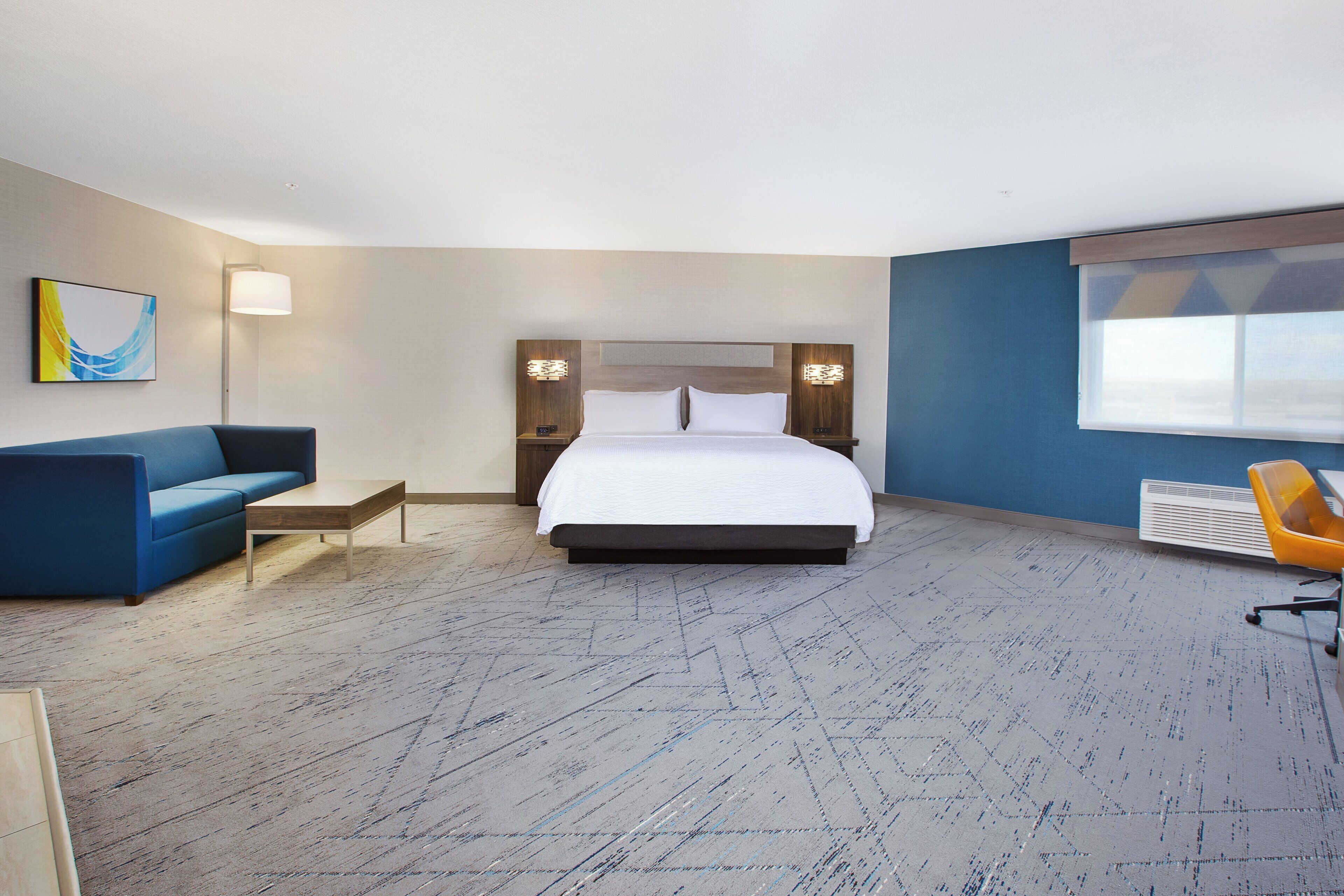 Quarto de hotel com uma cama, um sofá, uma escrivaninha e uma cadeira.