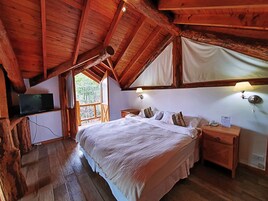 Quarto de cabana de madeira com cama, abajures, mesa de cabeceira de madeira e uma televisão sobre um móvel de madeira.