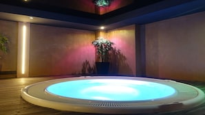 Uma banheira de hidromassagem em um quarto com piso de madeira, uma planta em vaso e uma parede com iluminação vertical.