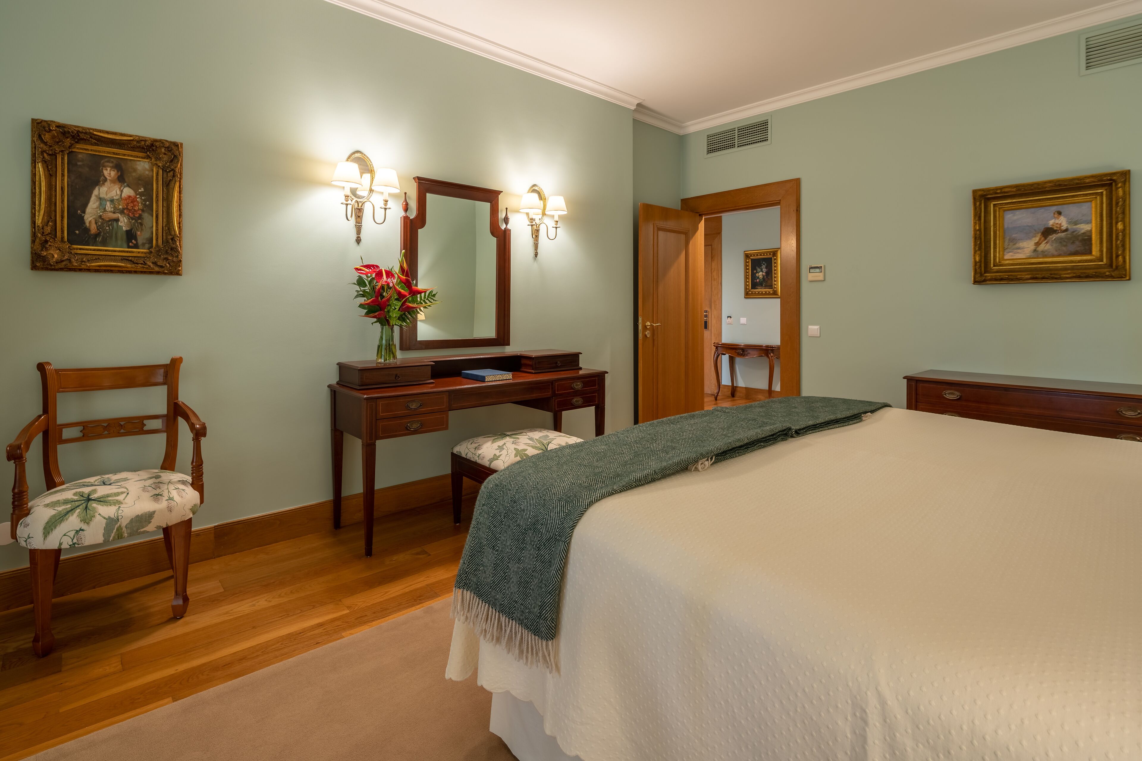 Quarto com cama, cômoda de madeira, cadeira, escrivaninha e espelho.